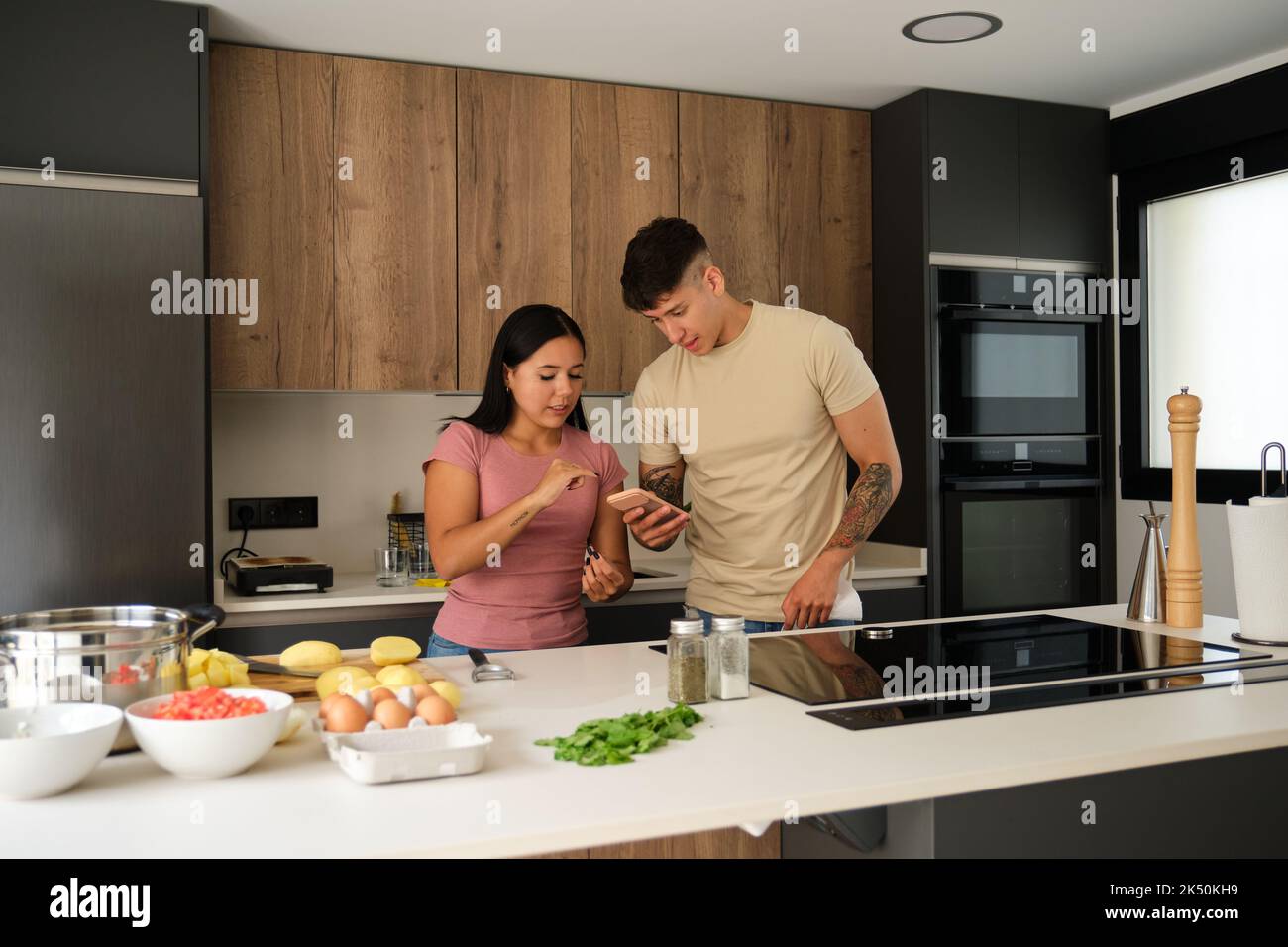 Two young latin people using the phone to check the recipe while ...