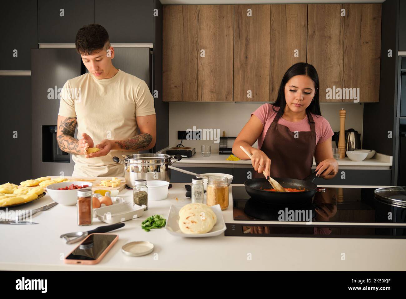 Two young latin people moulding llapingachos dough and cooking in a pan ...