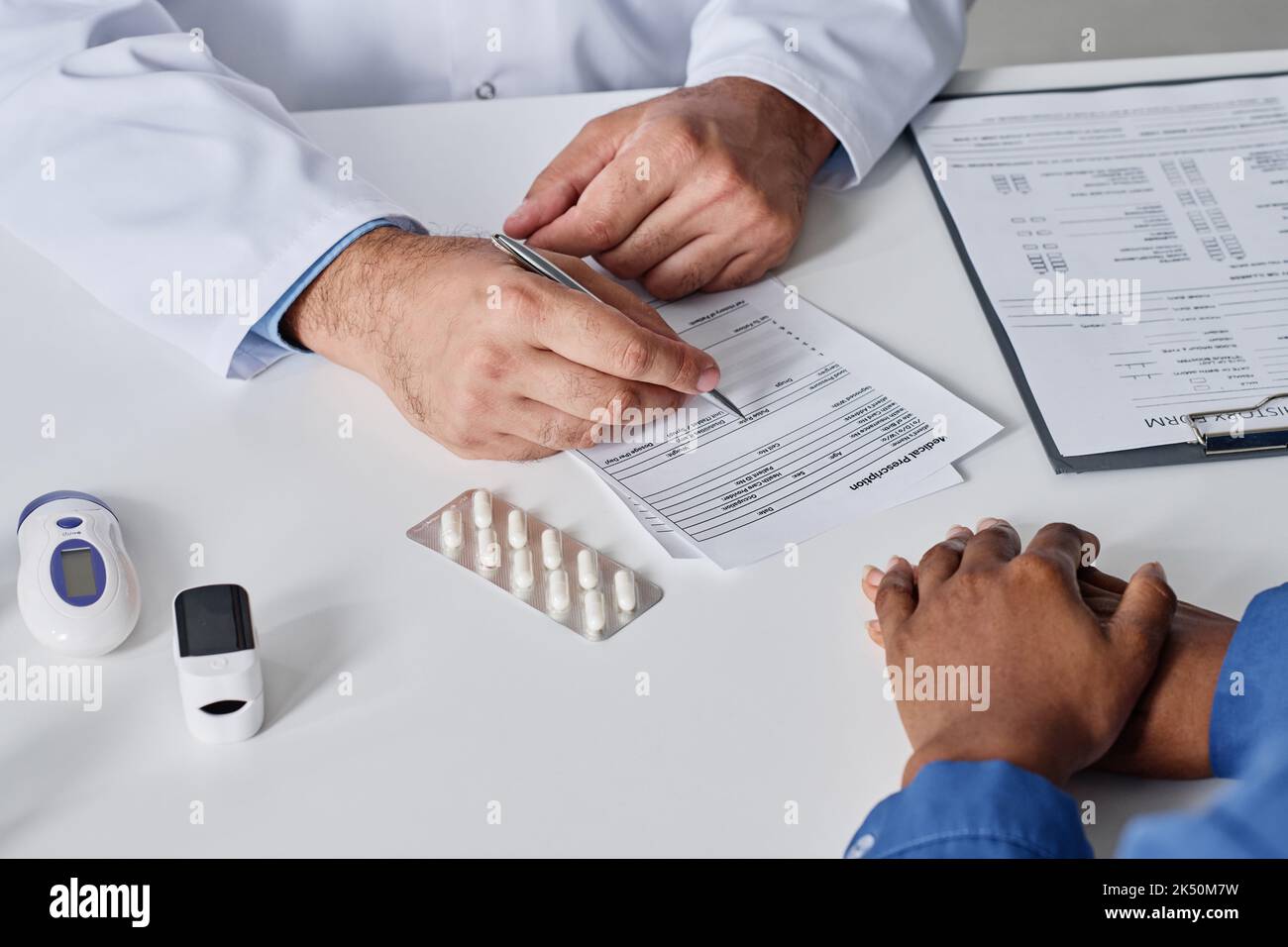 Close-up of doctor writing prescription for patient at table at office ...