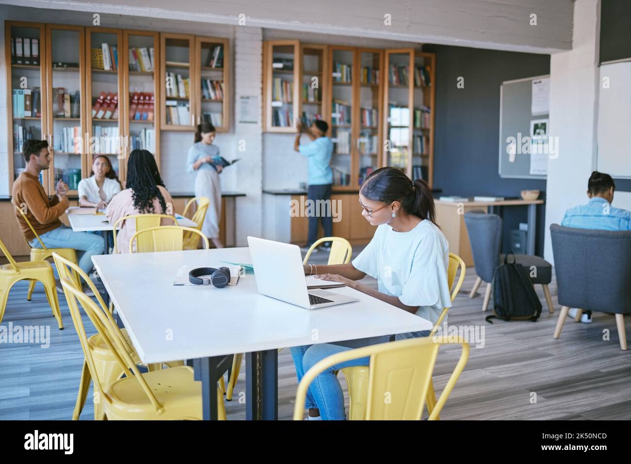 Students, laptop and modern library for education, learning and study ...