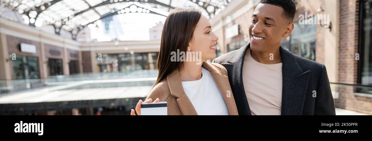 happy young woman holding credit card near trendy african american ...