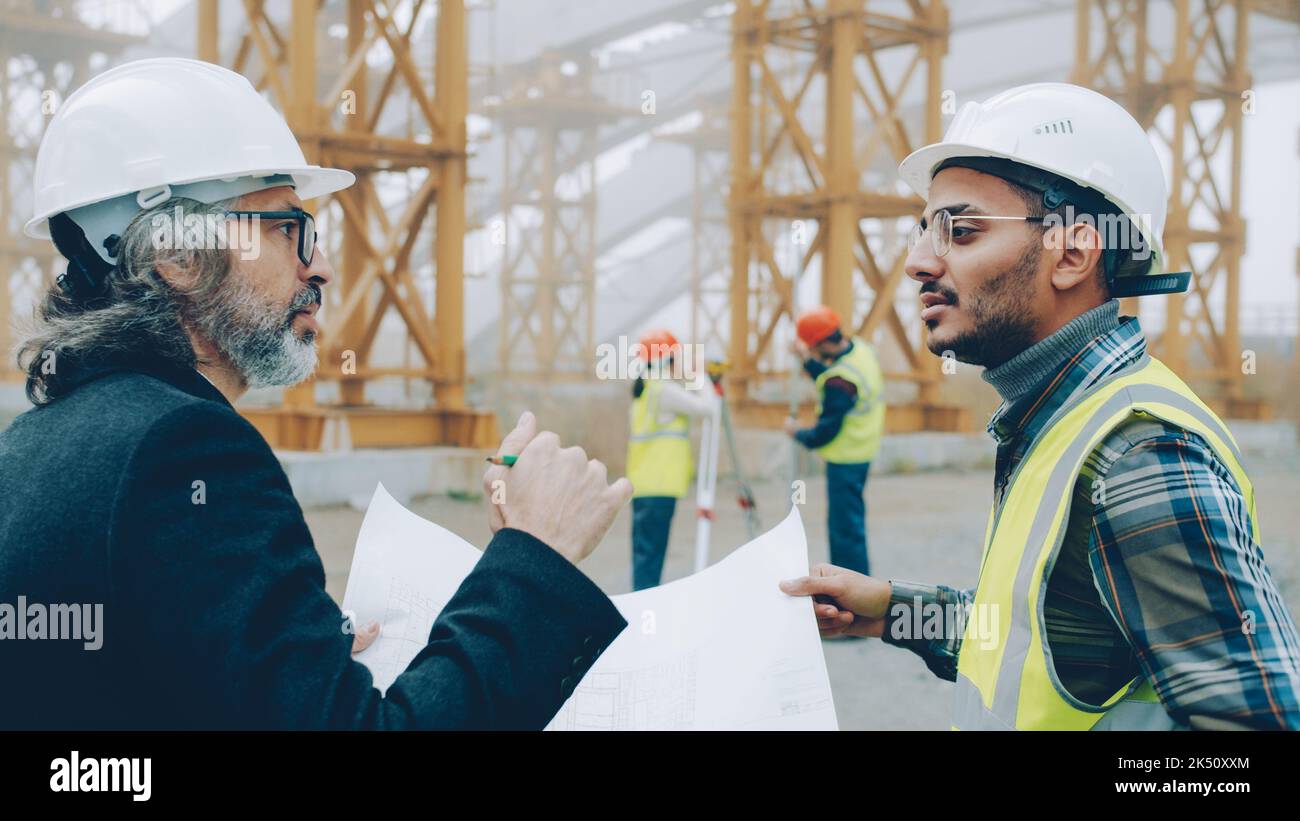 Foreman is discussing blueprints with project manager while surveyors ...