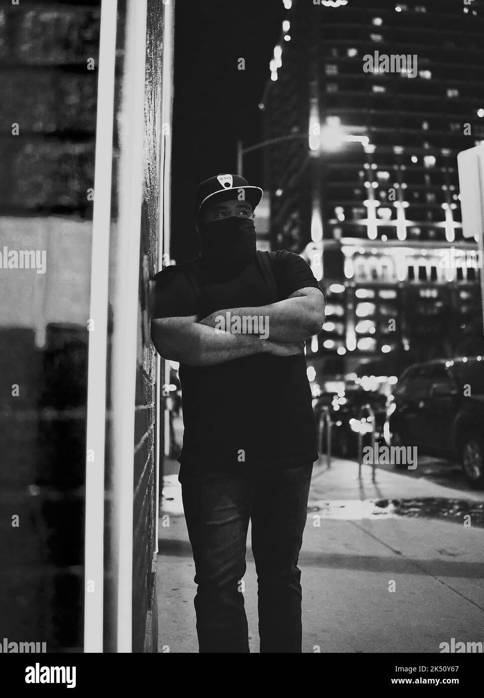 A vertical grayscale shot of a man in a cap with a covered face posing ...