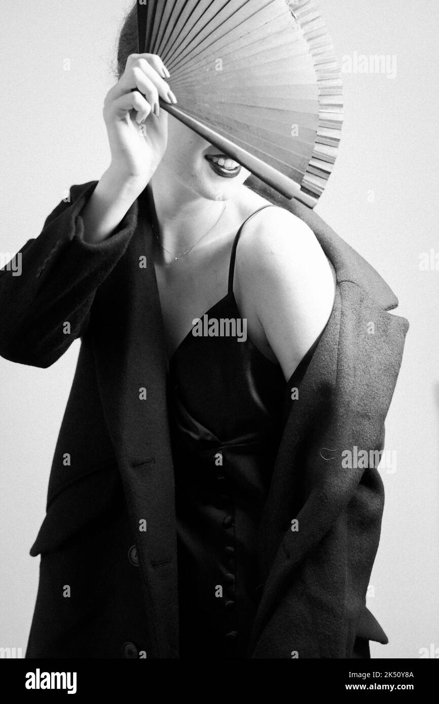 A vertical greyscale shot of an attractive female posing with a fan ...