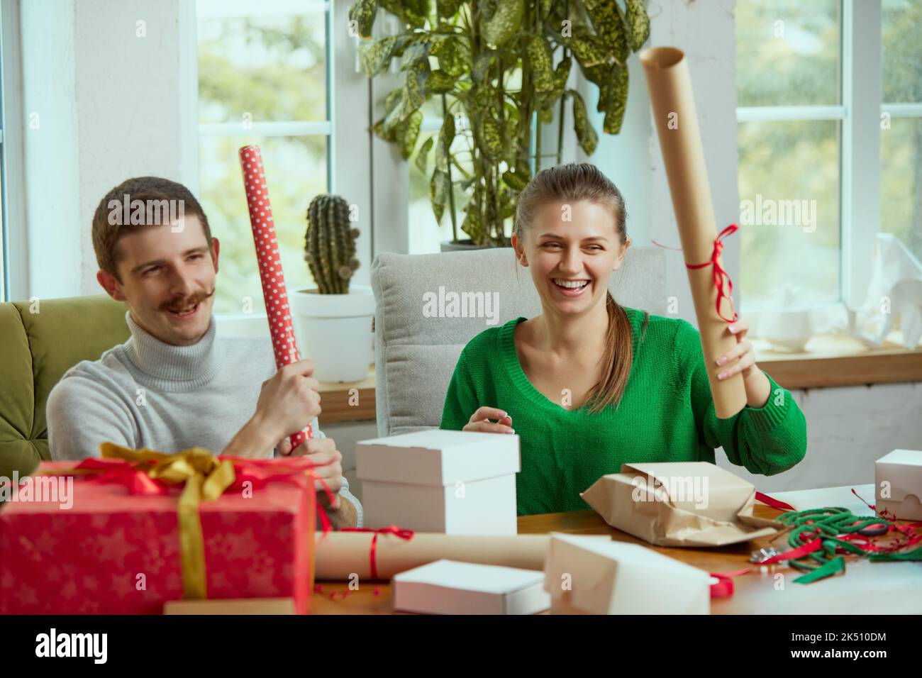 Portrait of cheerful young people, man and woman holding wrapping paper ...