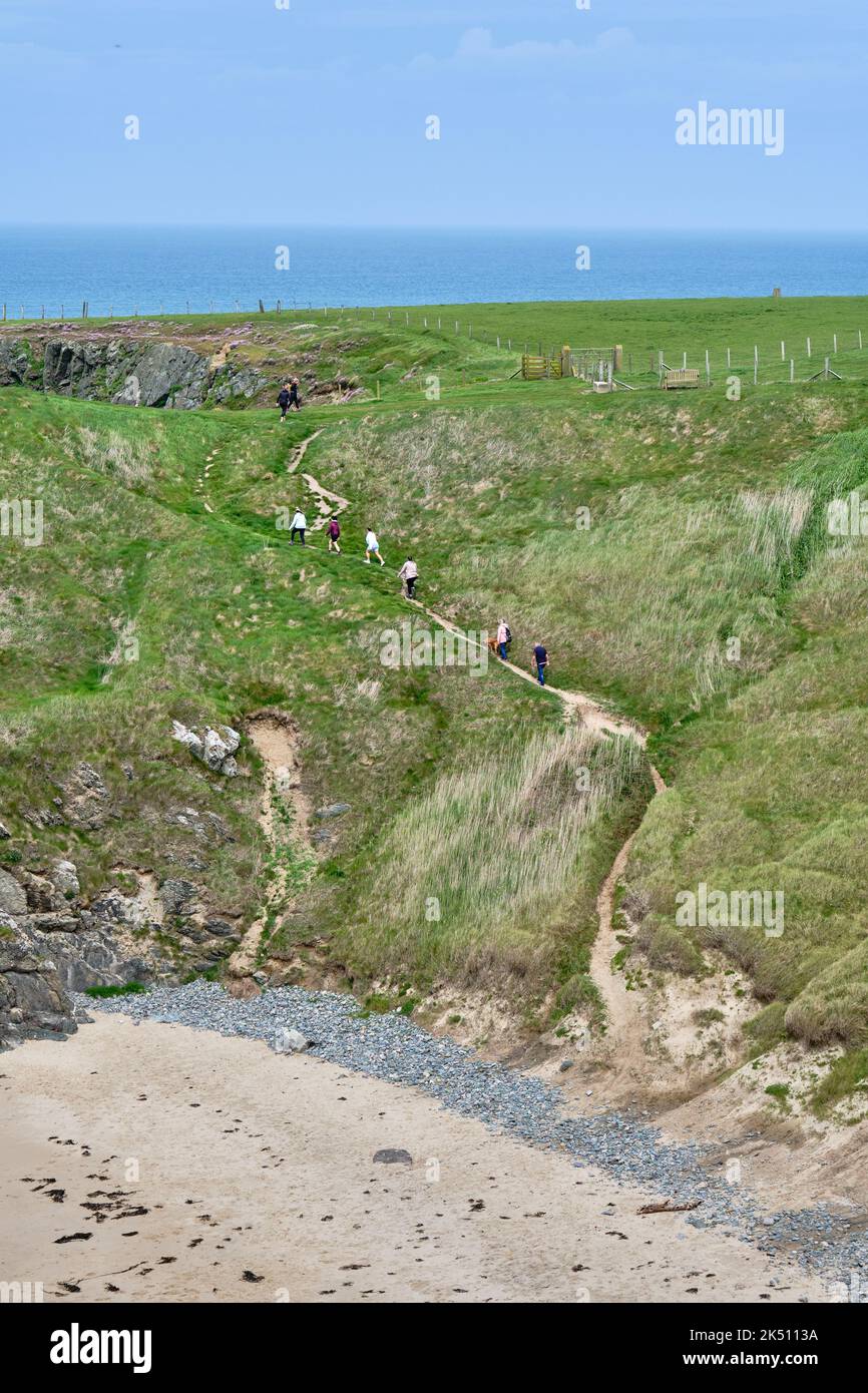 A group of people climbs the steep path up from the beach at Porth Lago ...
