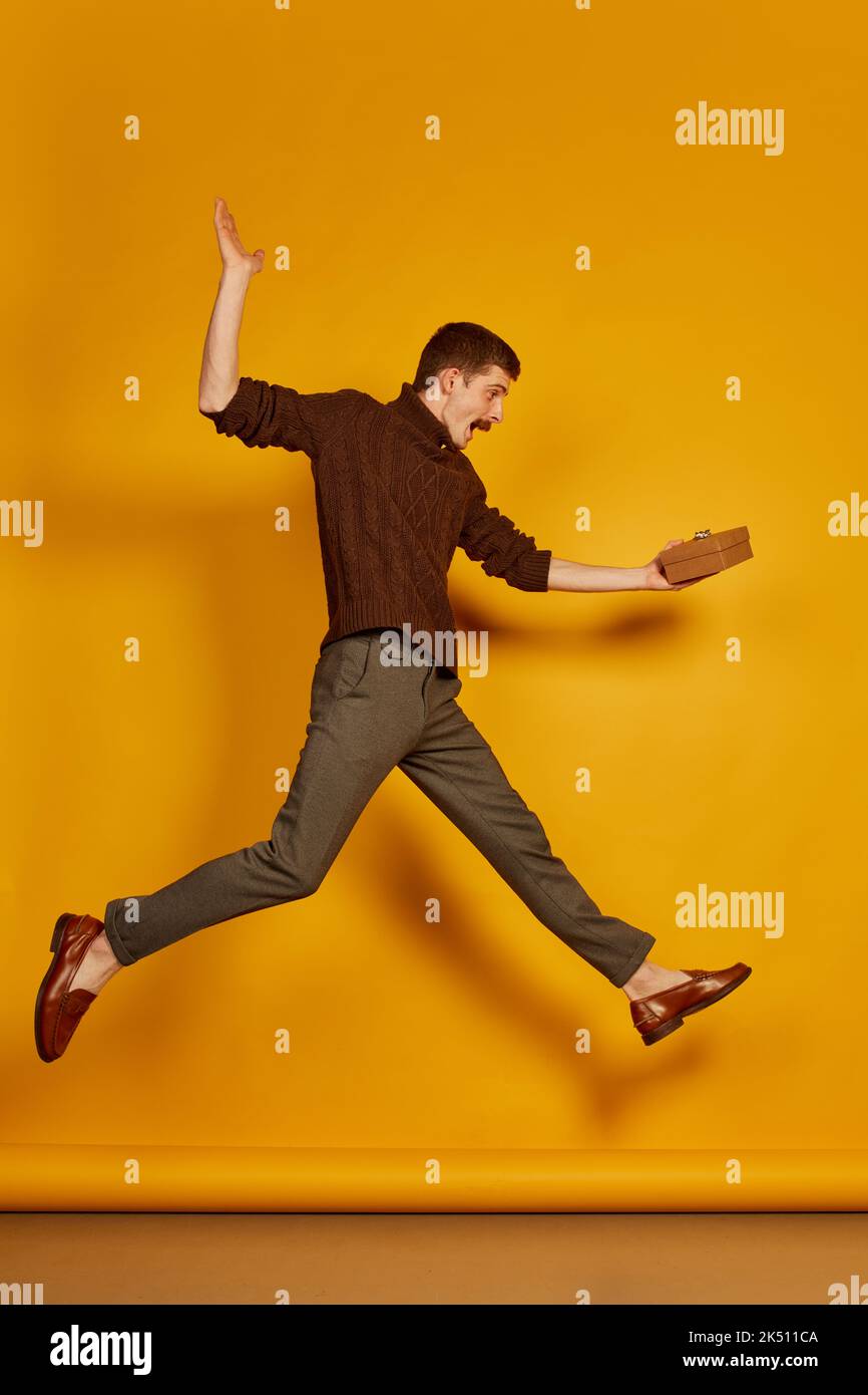 Portrait of young cheerful man jumping in joy with present box isolated ...