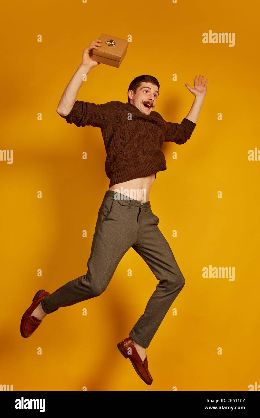 Portrait of young cheerful man jumping in joy with present box isolated ...