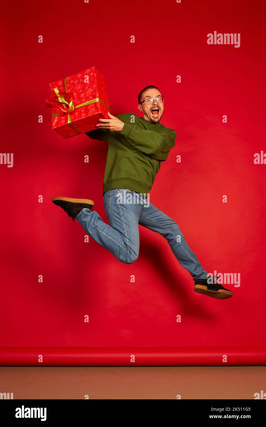 Portrait of young cheerful man jumping in joy with present box isolated ...