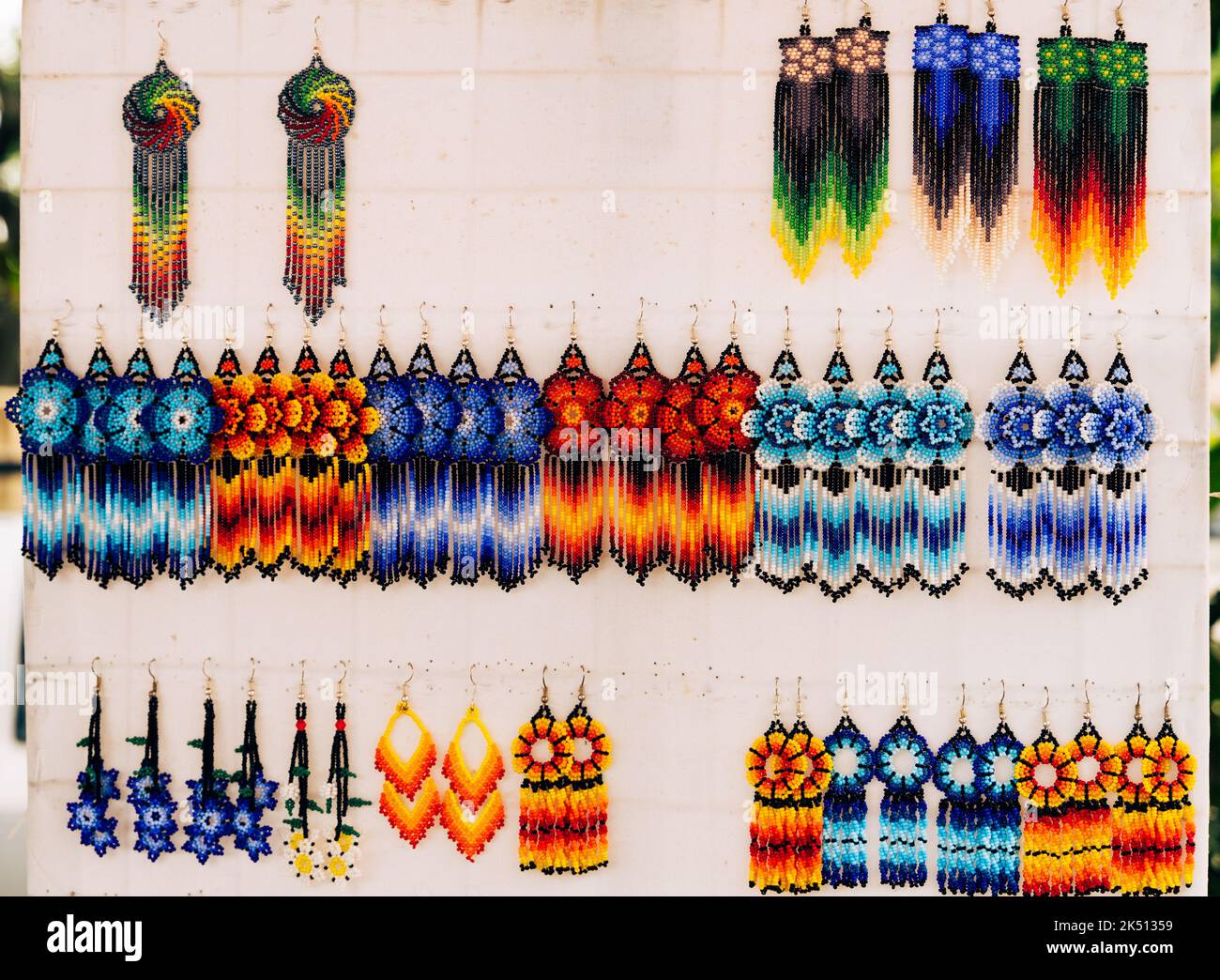 Colorful huichol earrings hanging on white display at market in Jalisco ...