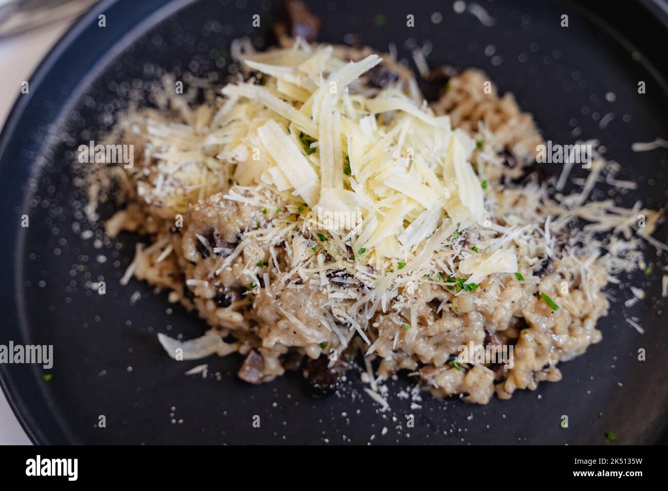 Grated parmesan cheese on top of mushroom risotto on black plate ...