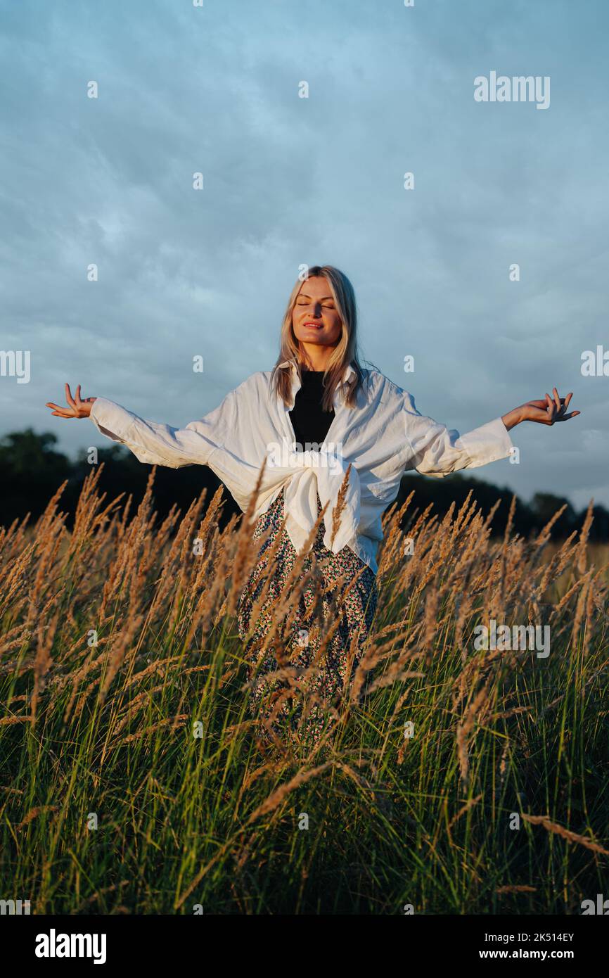 Meaditating young blond woman looking afar, standing amidst wheat field ...