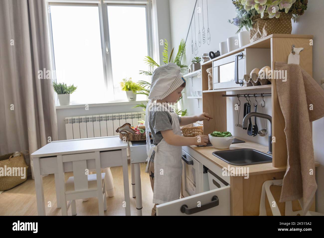 Cute little baby boy in chef hat and apron playing at childish kitchen ...