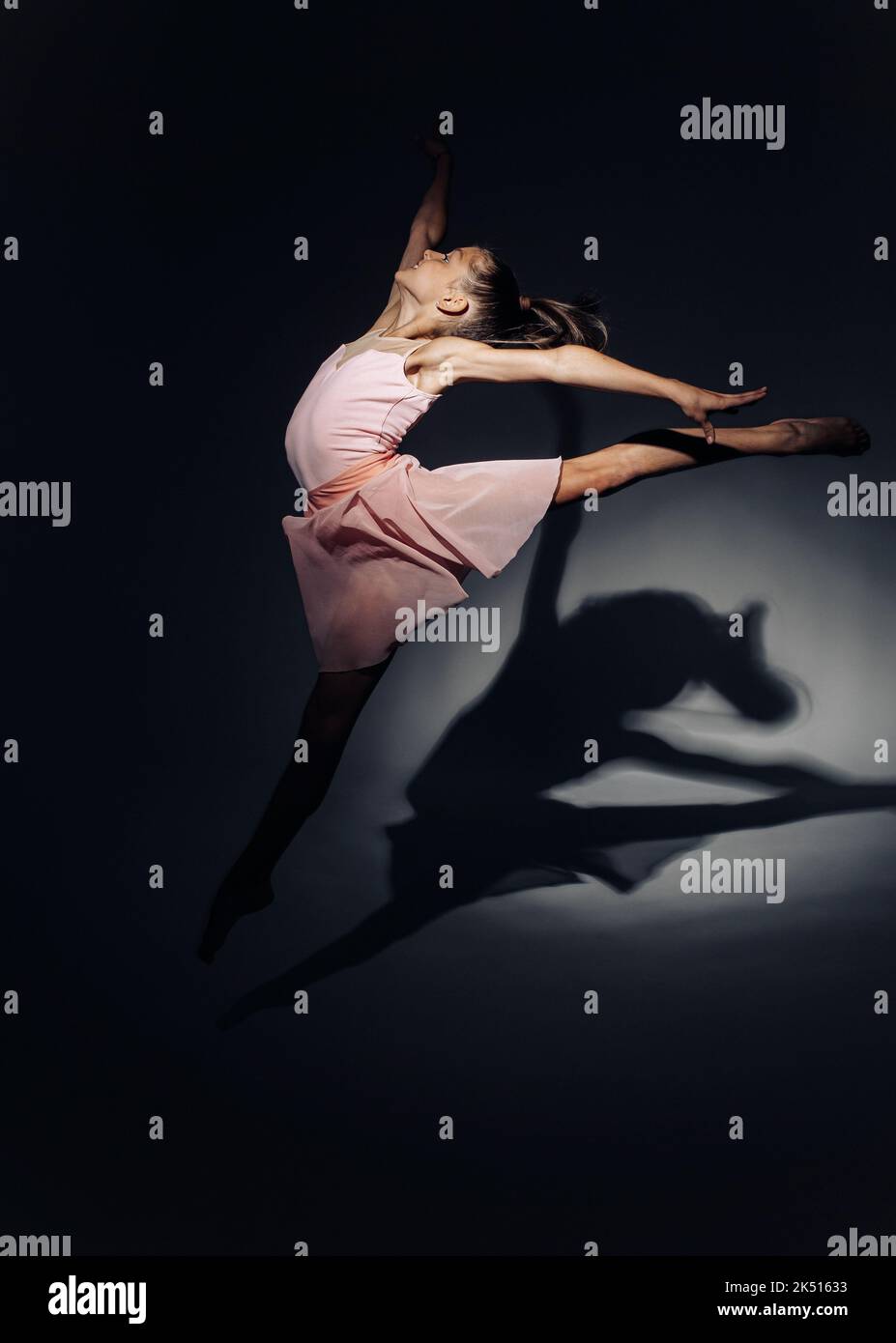 Ballerina child girl in pink dress dances lit by light on dark ...