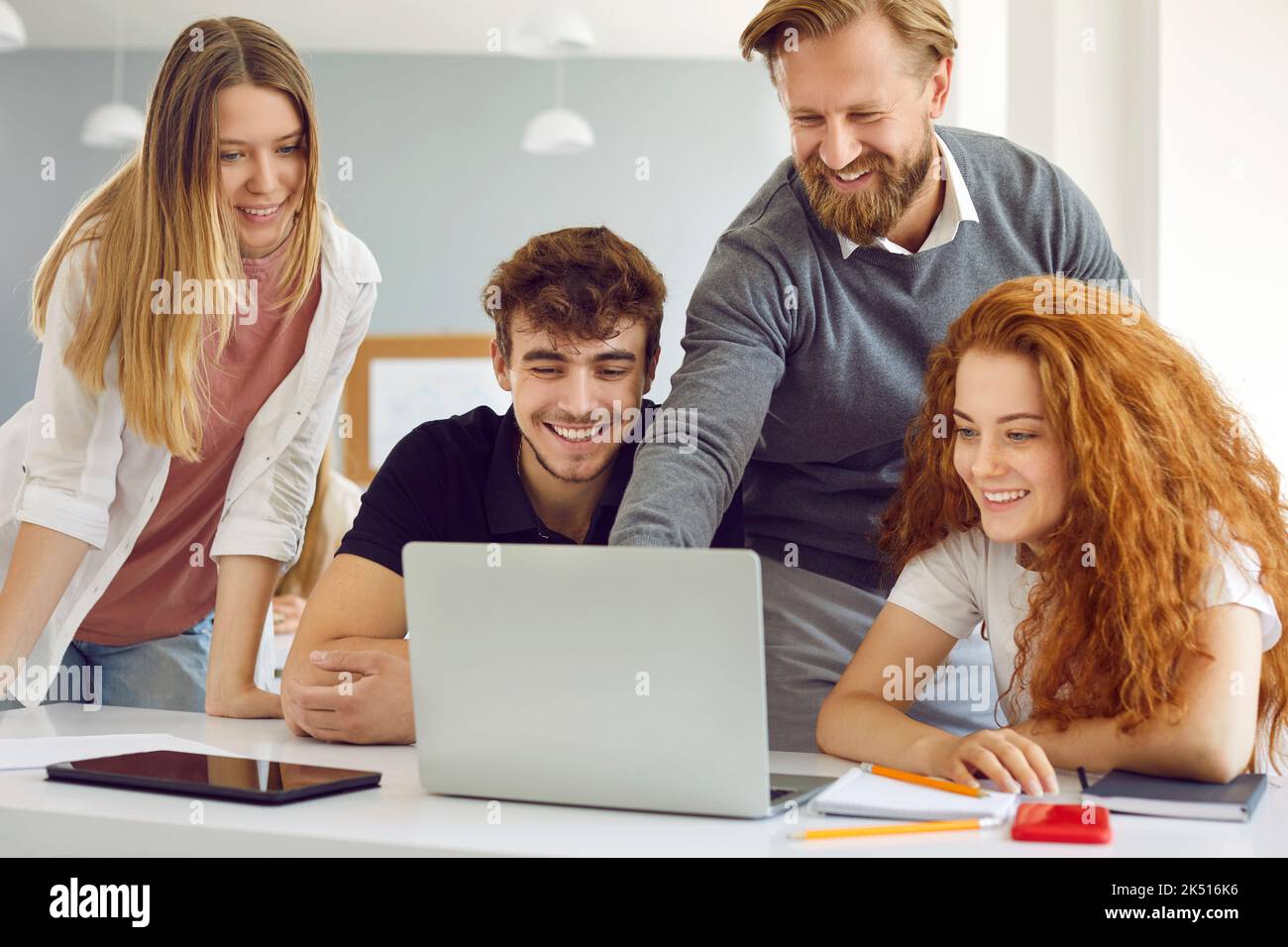 Male teacher helps group of college students working on laptop during ...