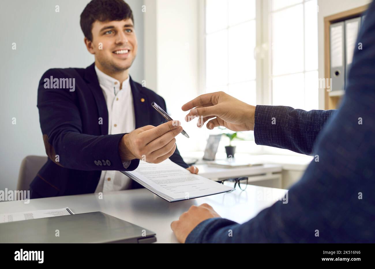 Happy agent hands over a contract and a pen to his client and asks him ...