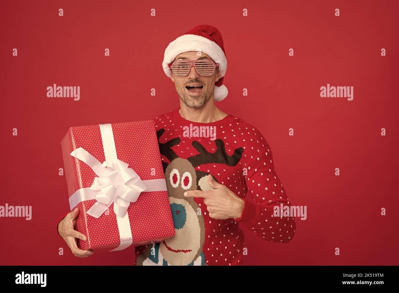 amazed xmas guy point finger on present box on red background. happy ...