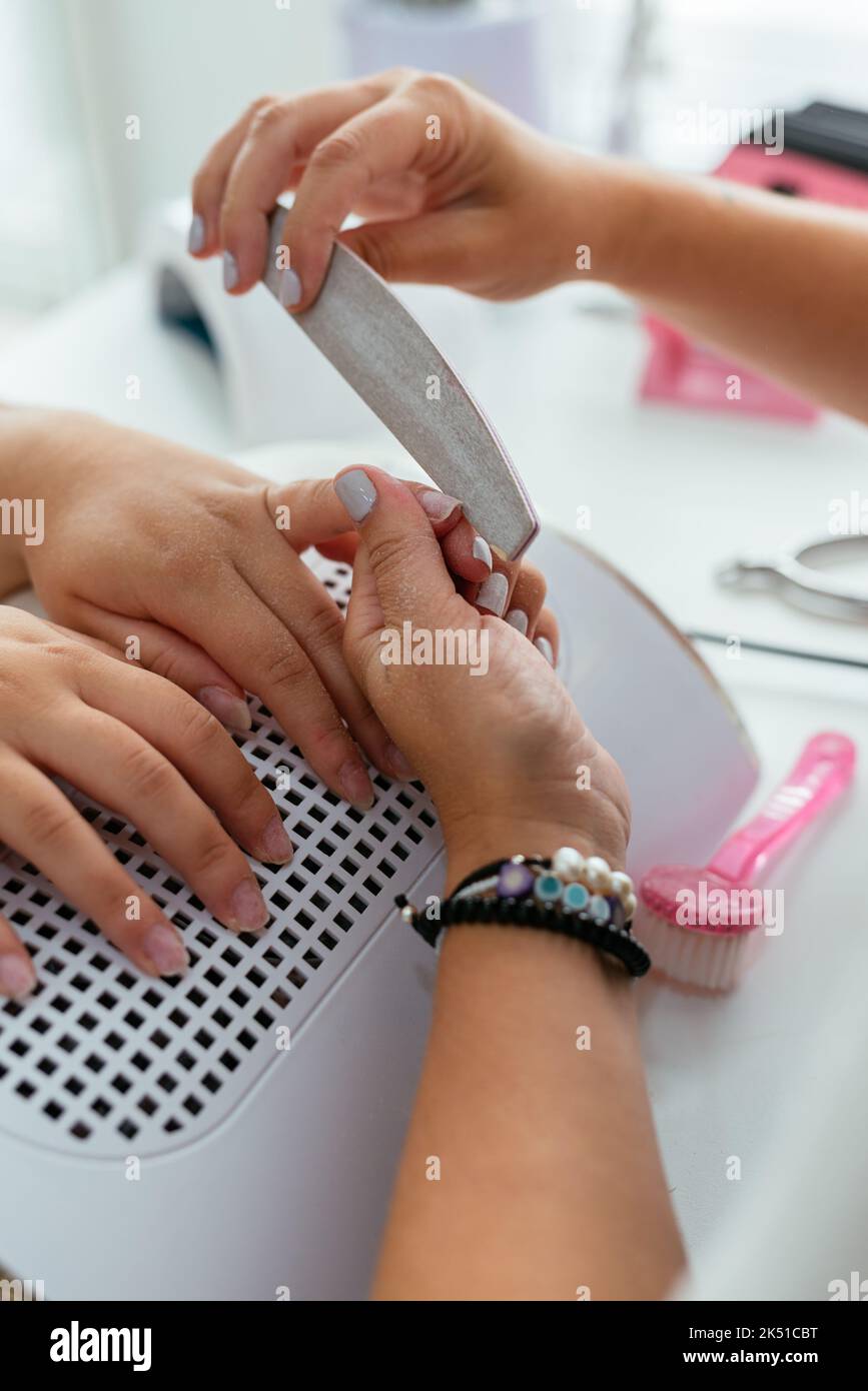 Adult female manicurist filing nails of crop anonymous client during ...