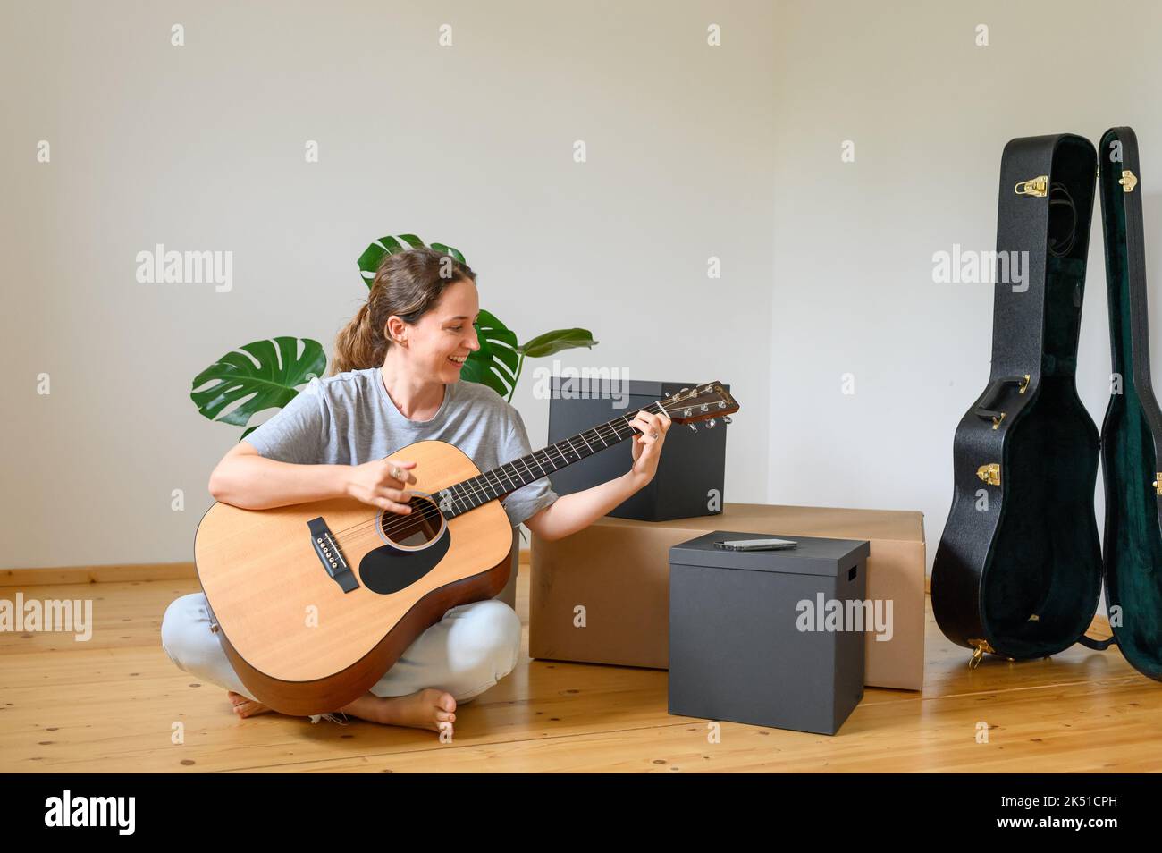 Merry young female musician smiling and playing guitar while sitting ...