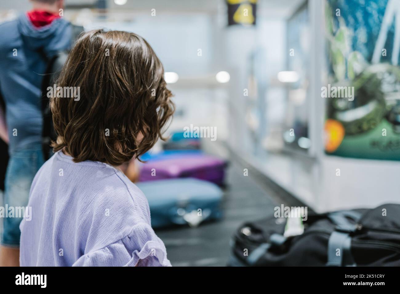 Back view of unrecognizable girl in lilac clothes waiting for luggage ...