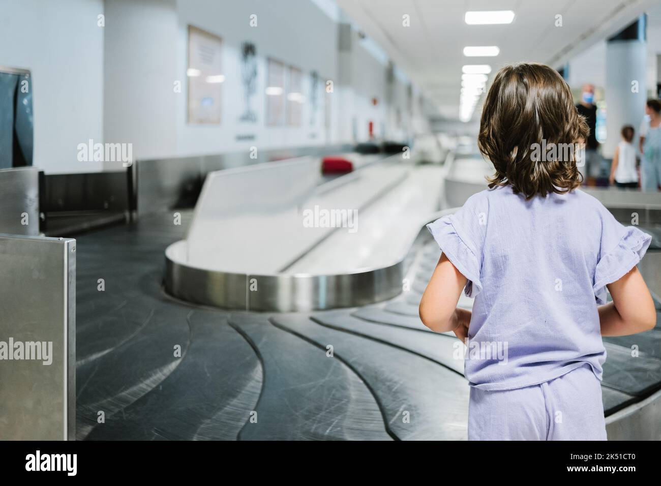 Back view of unrecognizable girl in lilac clothes waiting for luggage ...