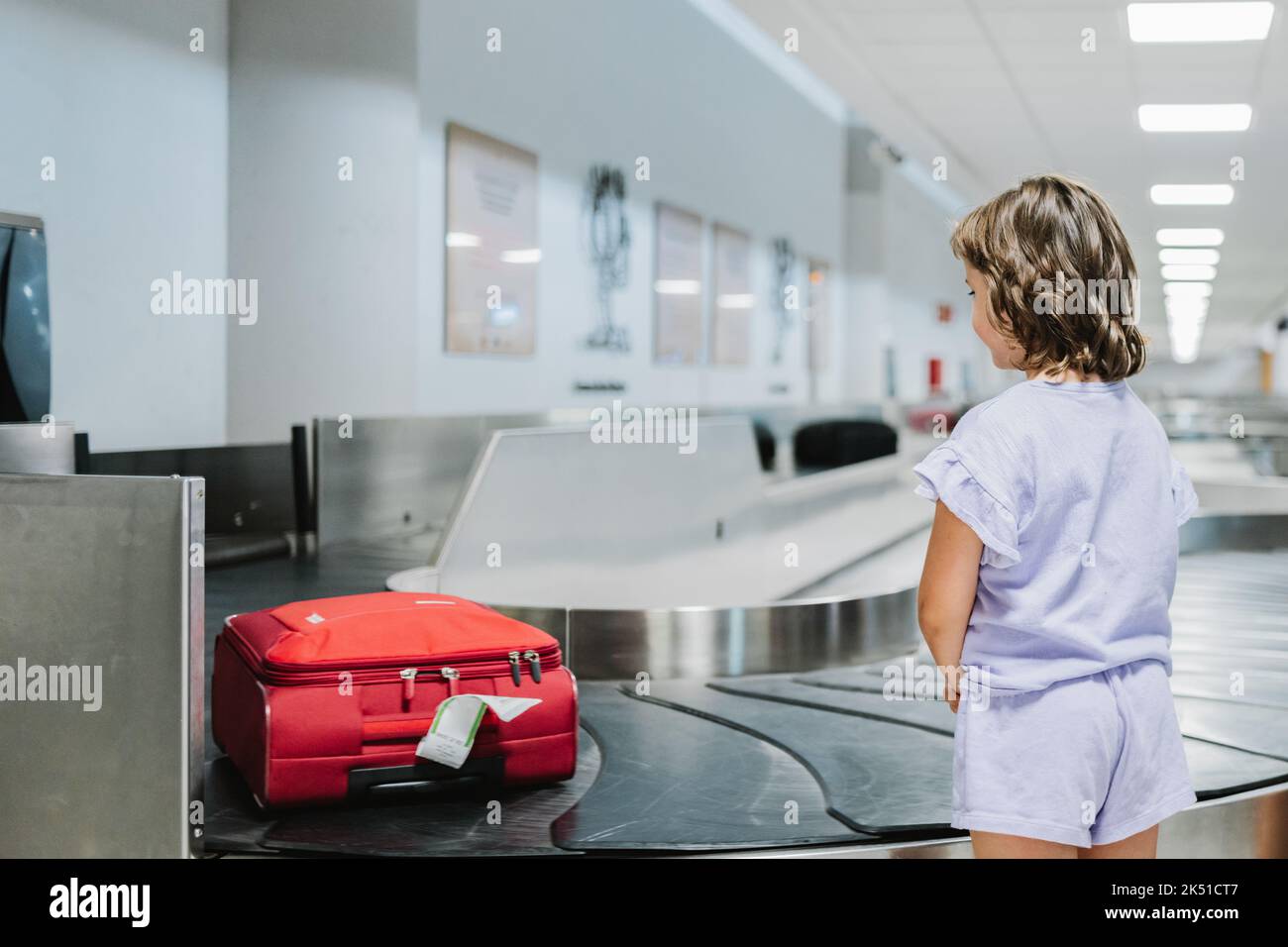 Back view of unrecognizable girl in lilac clothes waiting for luggage ...