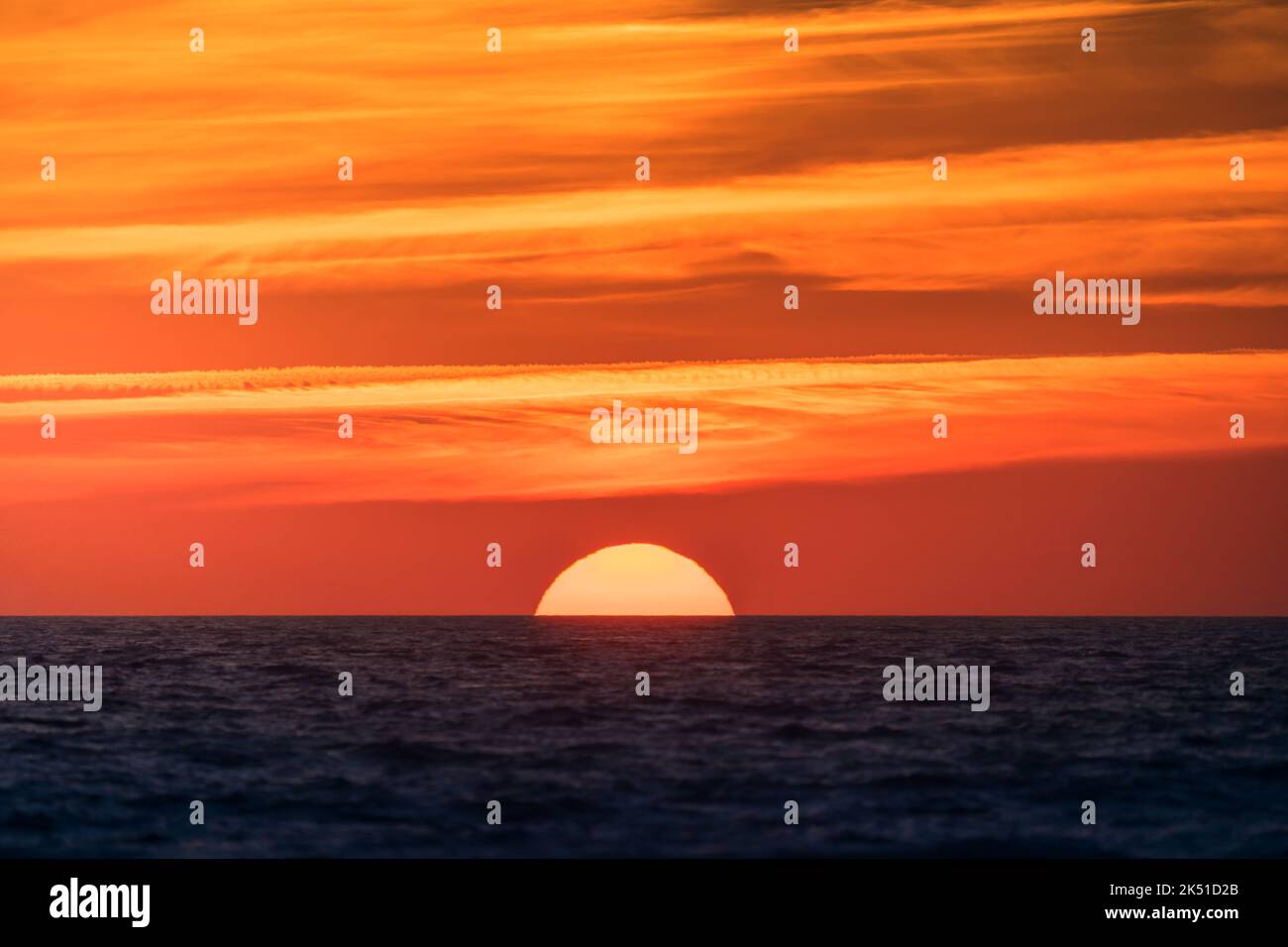 Glowing semi circle of setting sun on horizon line with dark rippling ...