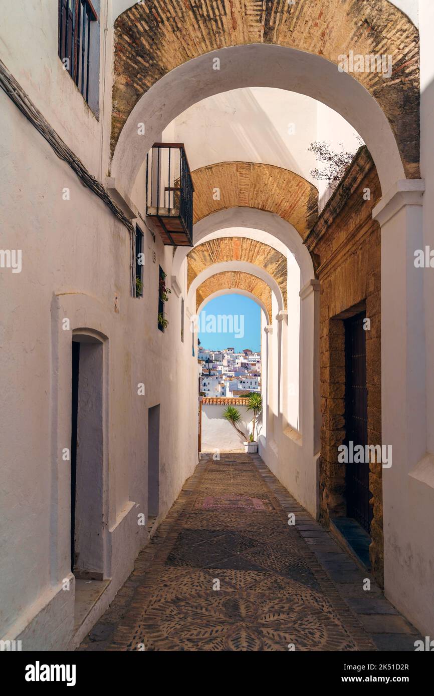 Narrow stone paved street with brick and white plastered arcs above ...