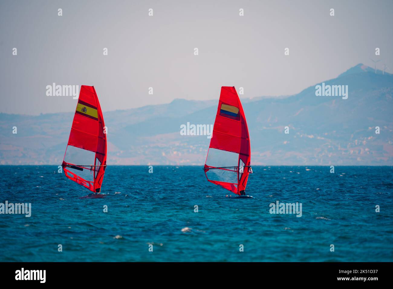 Red sails of windsurfers on rippling blue water of sea bay with blurred ...