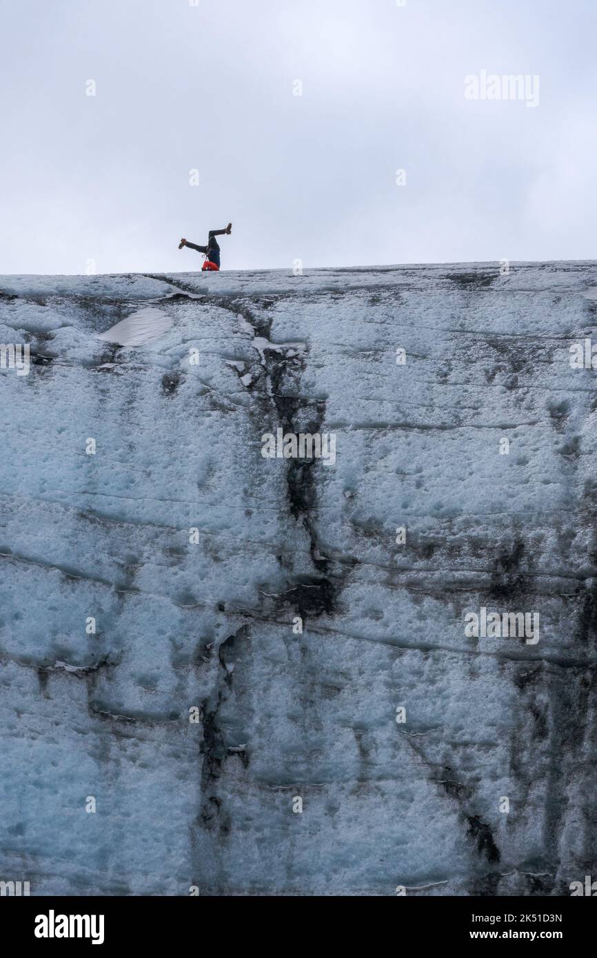 Anonymous tourist in outerwear doing headstand on top of Vatnajokull ...