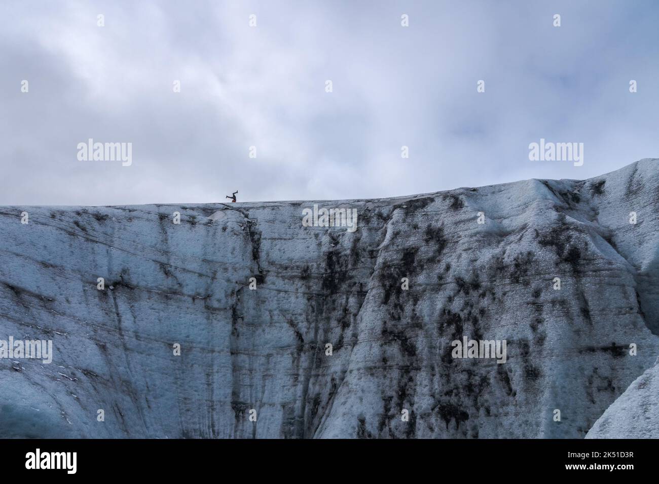 Anonymous tourist in outerwear doing headstand on top of Vatnajokull ...