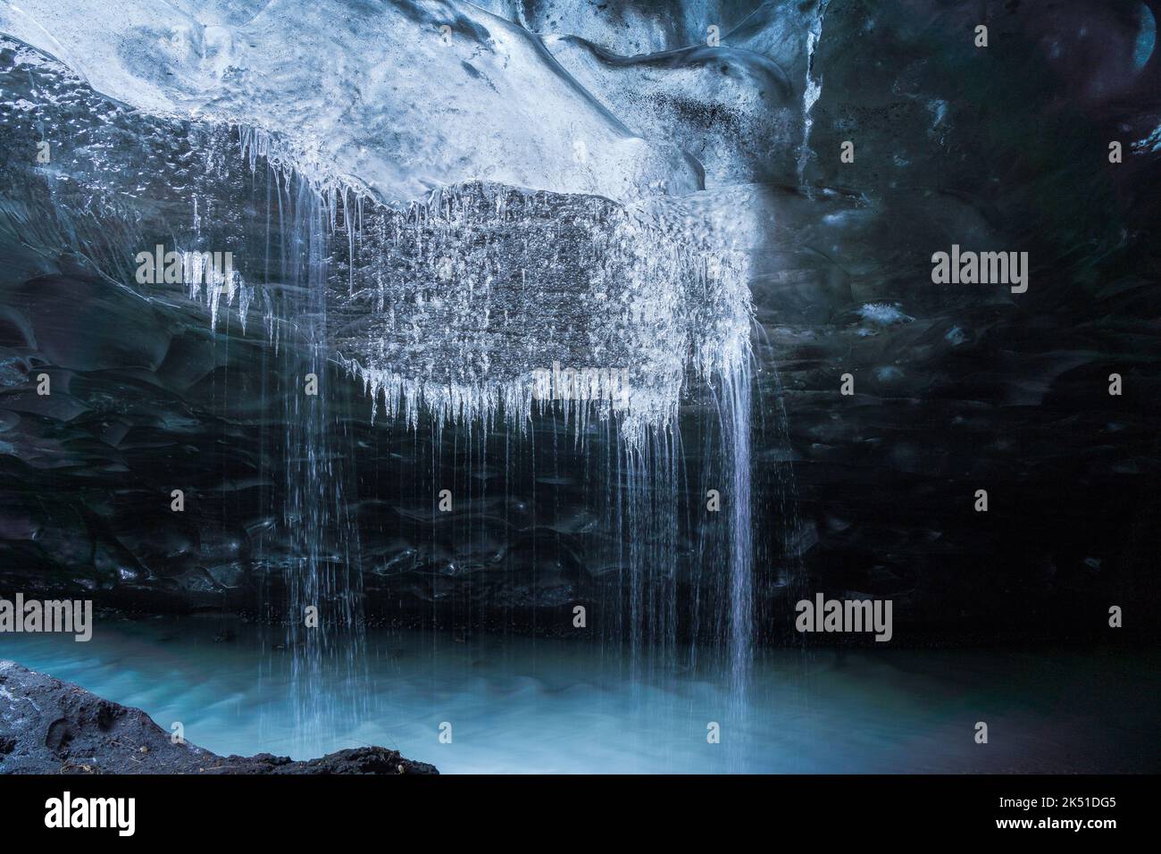 Clean water falling from fragile transparent icicles into blue stream ...