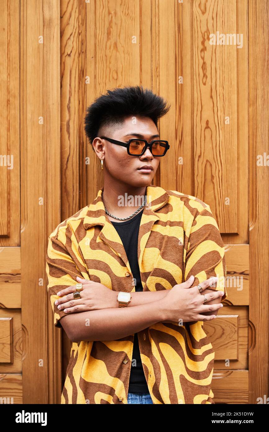 Stylish serious young non binary male in bright shirt and sunglasses ...