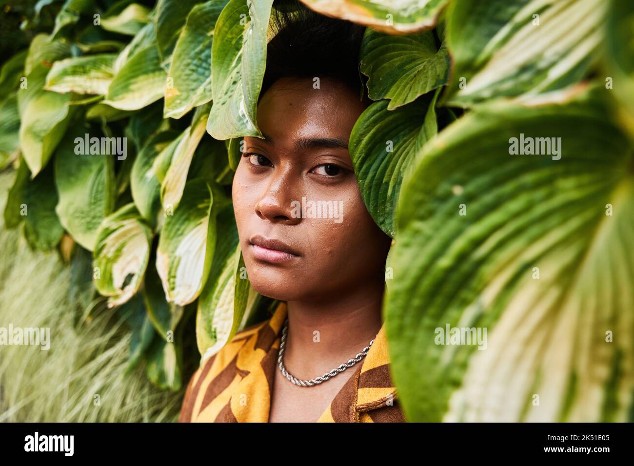 Dreamy thoughtful young Filipino non binary man wearing cool shirt with ...