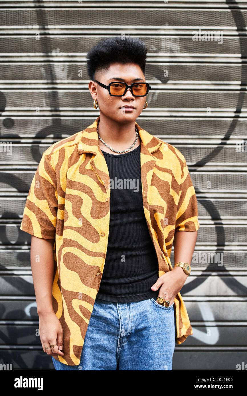 Stylish serious young non binary male in bright shirt and sunglasses ...