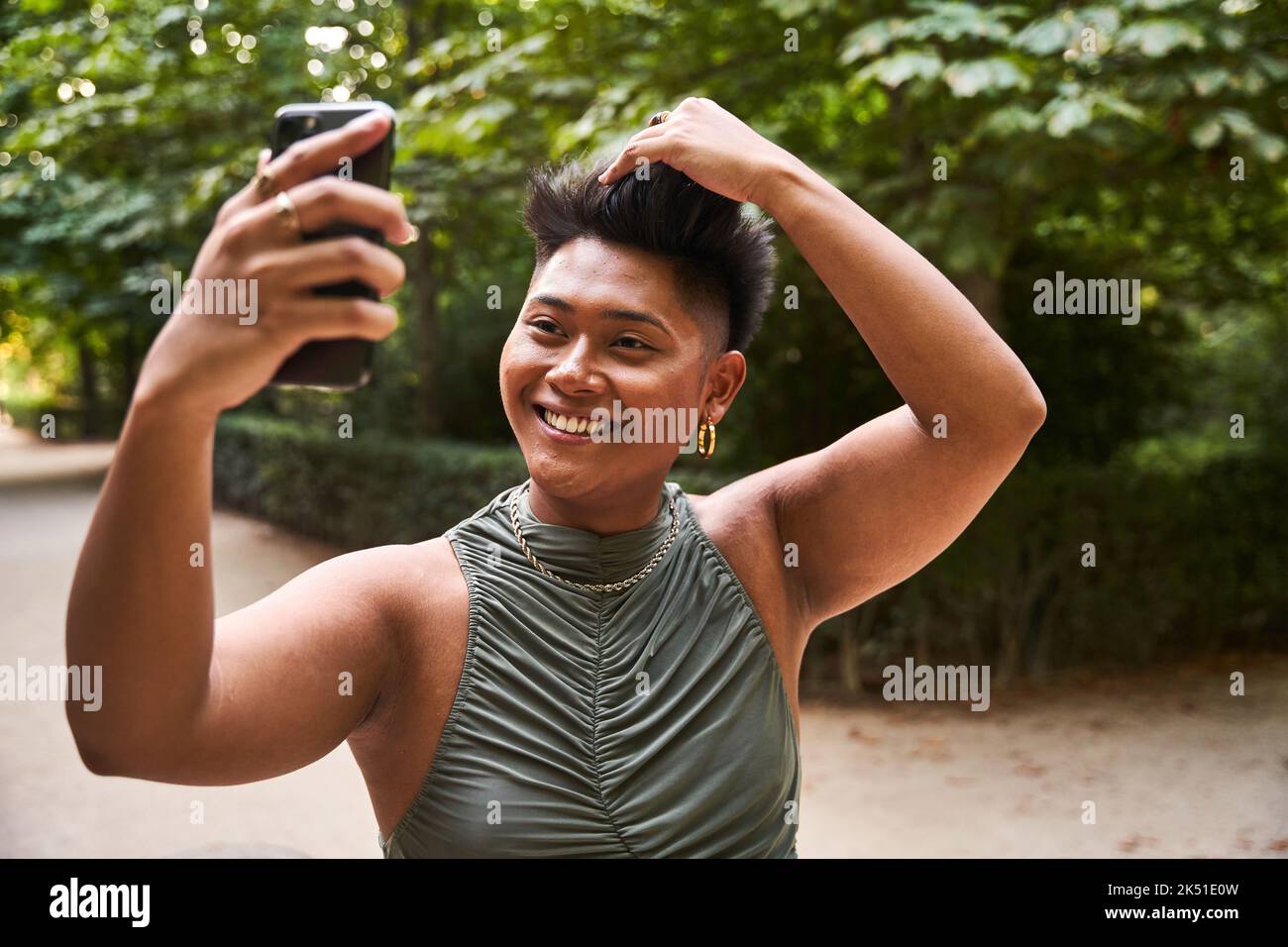 Happy Filipino transgender woman smiling and touching short hair while ...