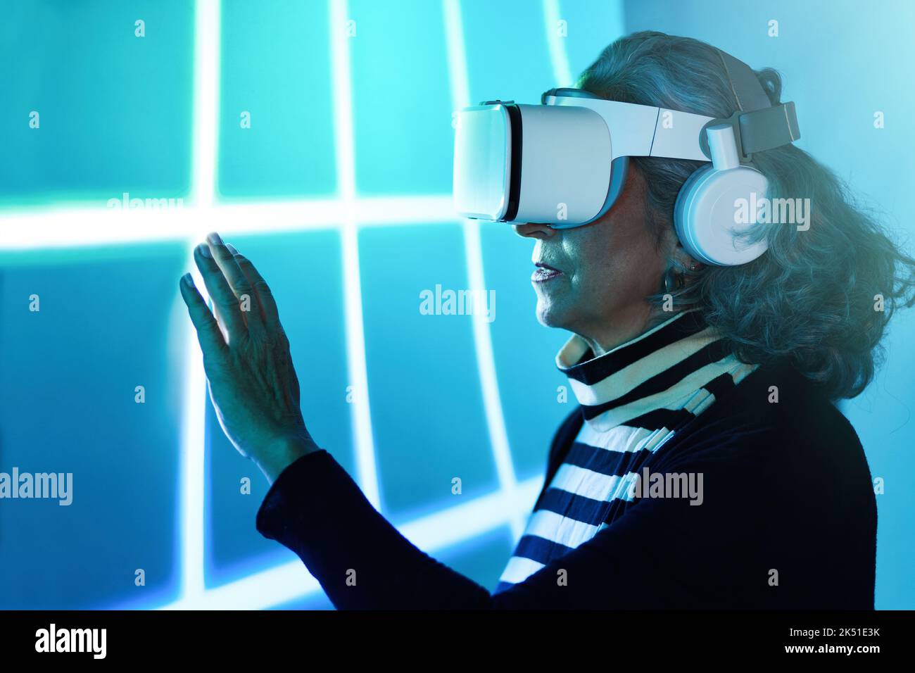 Elderly female in VR glasses and headphones touching neon mesh while ...