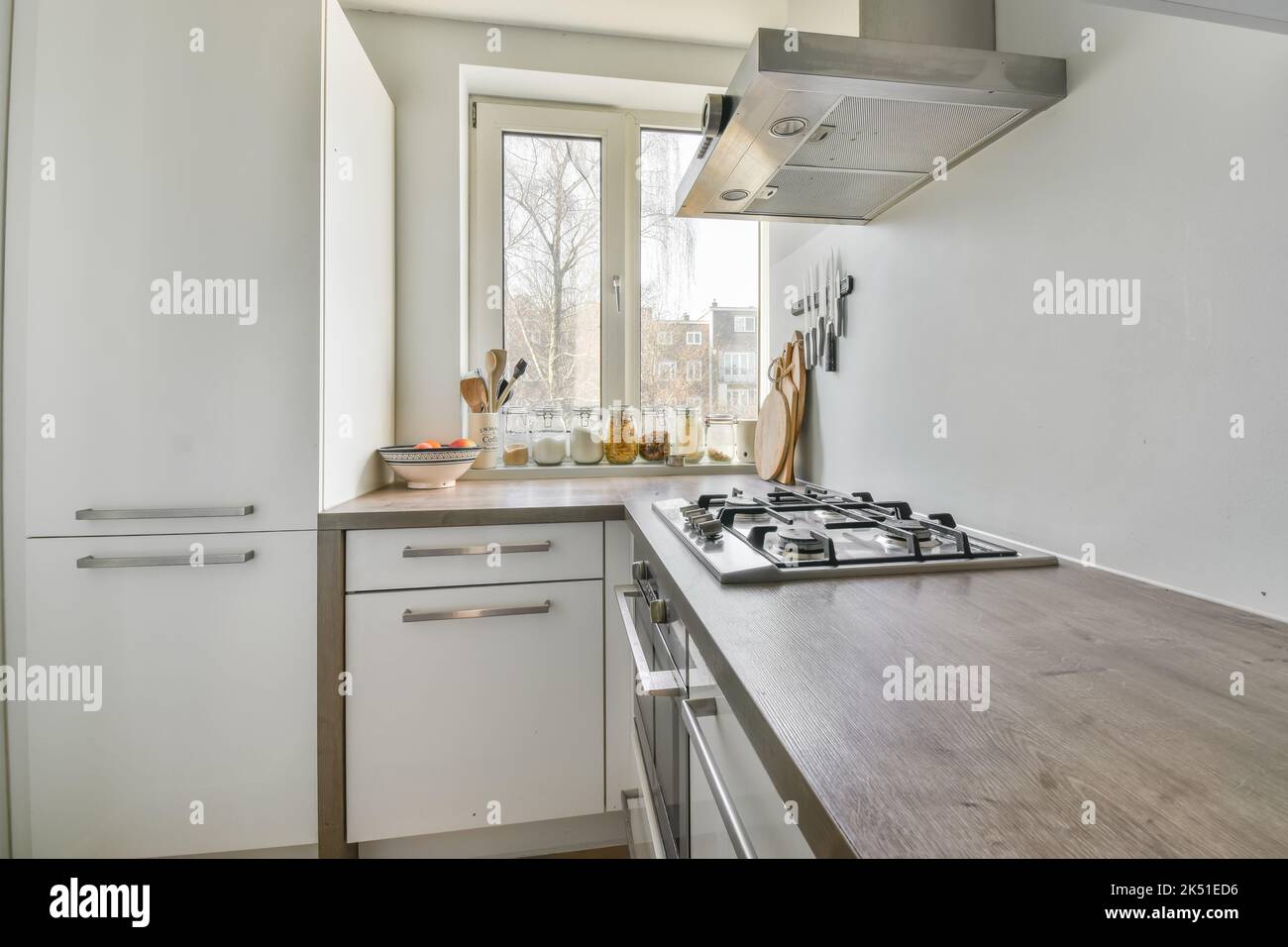 Wooden counter with cooker and utensils placed in light spacious ...
