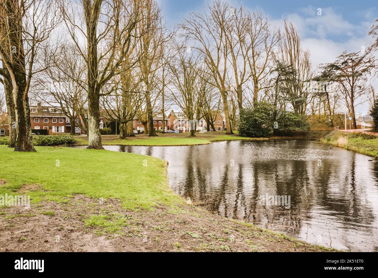 Lake next to some trees and houses under blue sky with clouds Stock Photo - Alamy