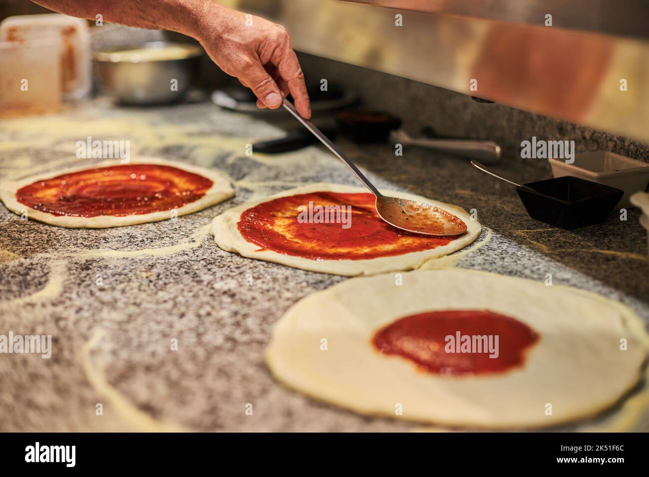 Anonymous man using spoon to smear tomato sauce on pizza bases while ...