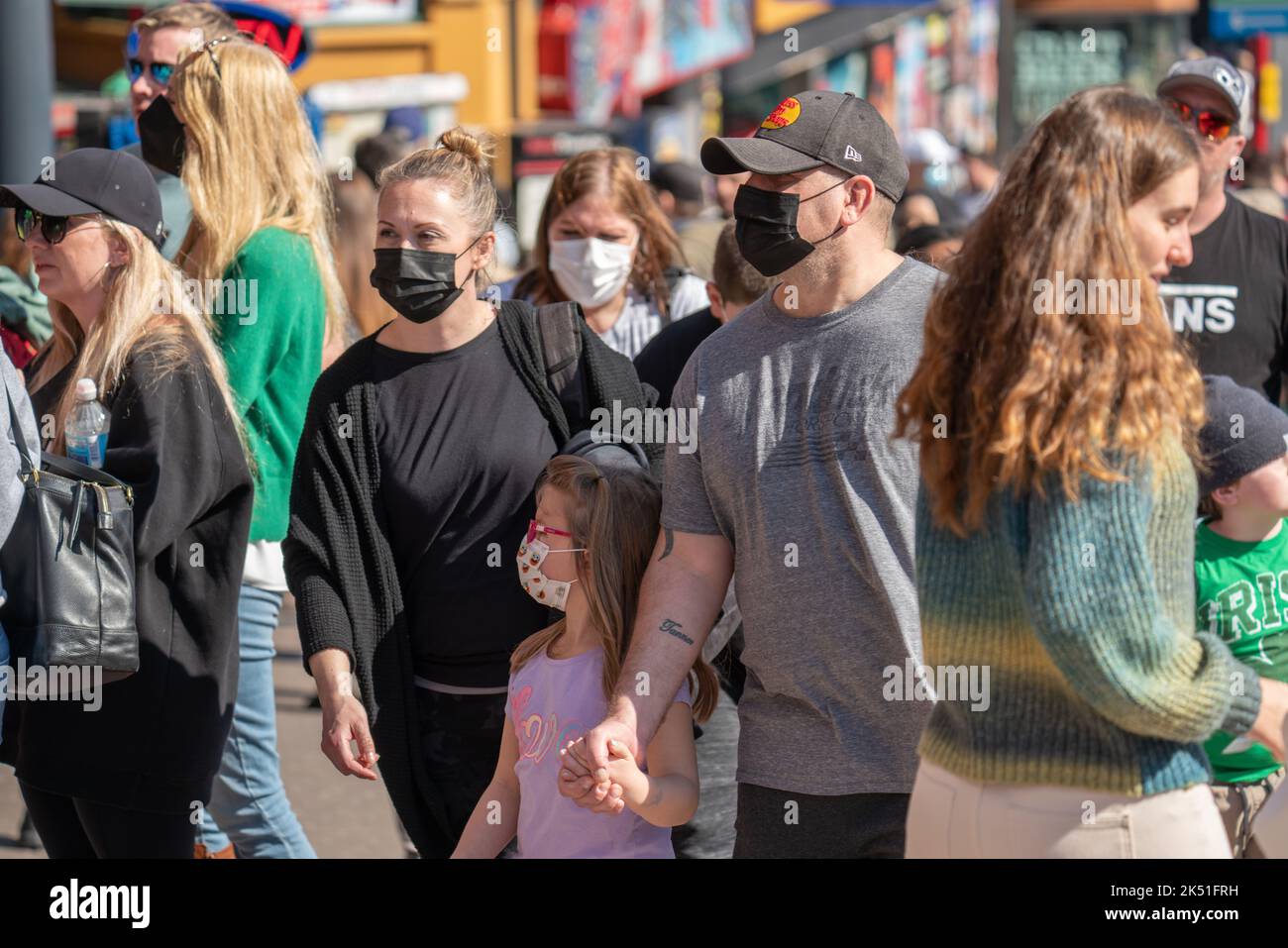 Crowds of people walking down Clifton Hill street wearing black covid ...