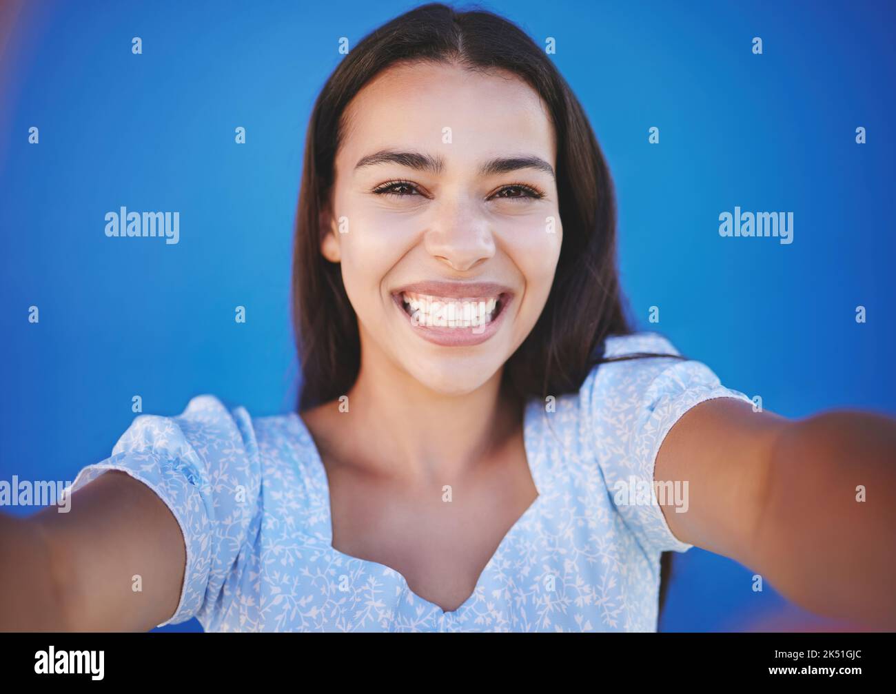 Portrait of girl taking a selfie with blue background and smile on face ...