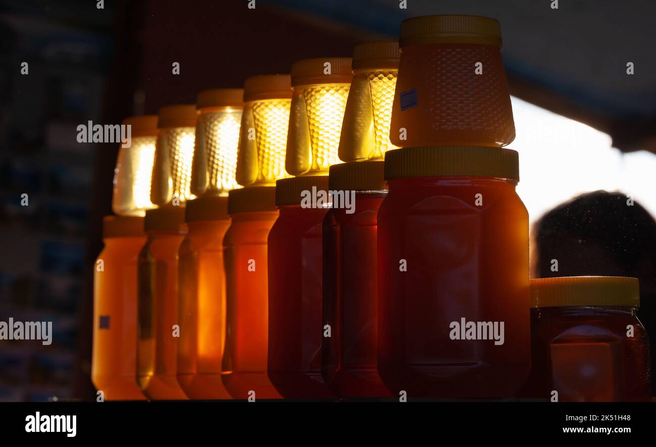 Jars of natural honey stand on a shop window in a row. Close up photo ...