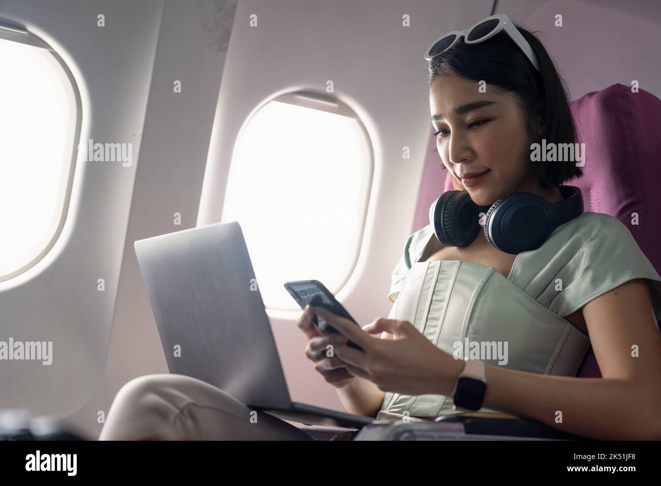Attractive asian woman passenger of airplane read news from networks via smartphone and wifi on ...