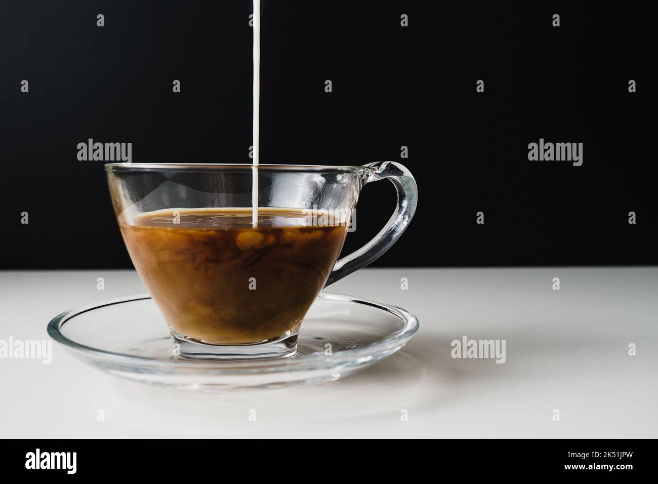 Milk being poured into coffee cup. Set against a black background with ...