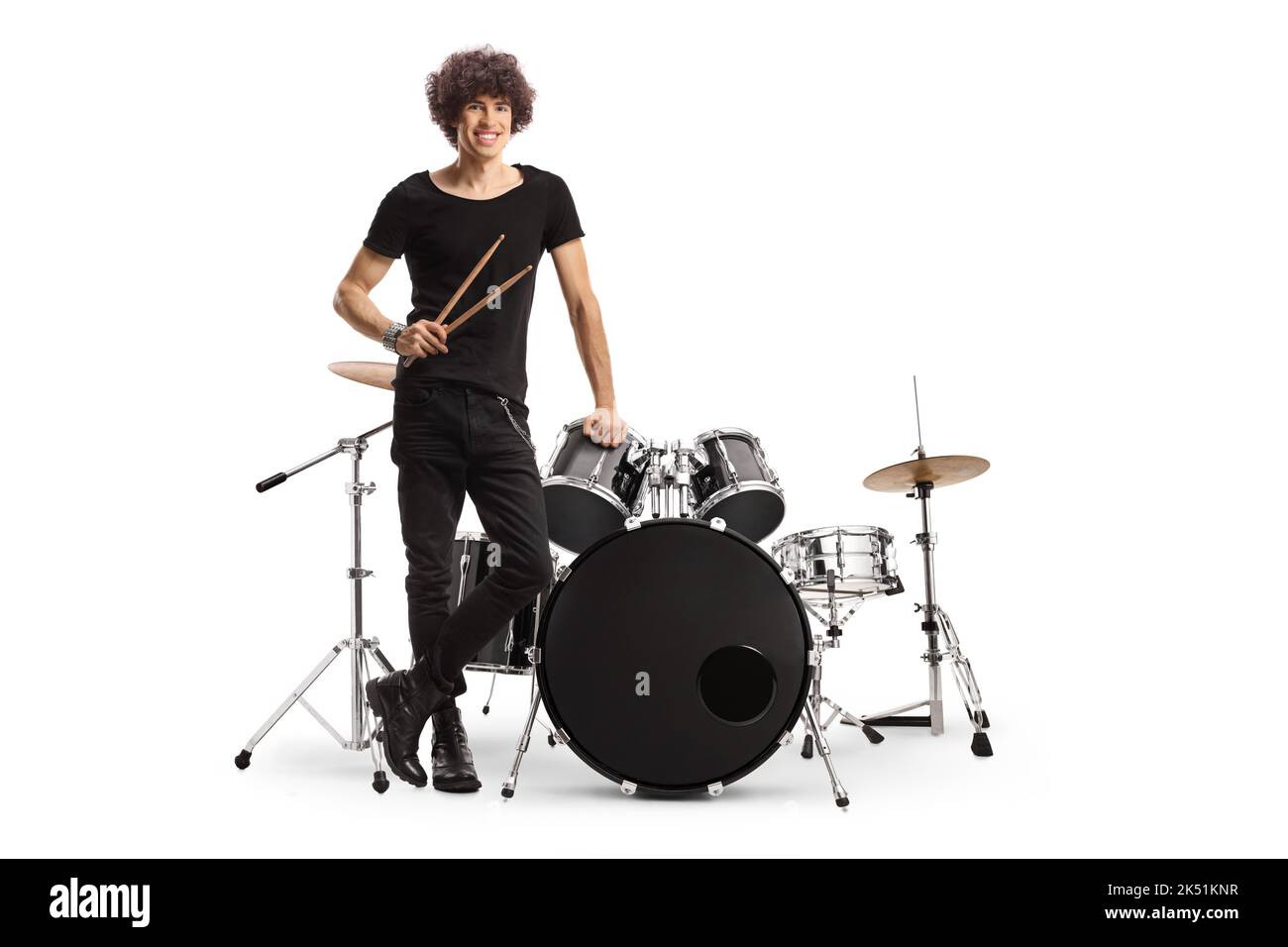 Young male drummer standing next to a drum kit and holding drumsticks ...