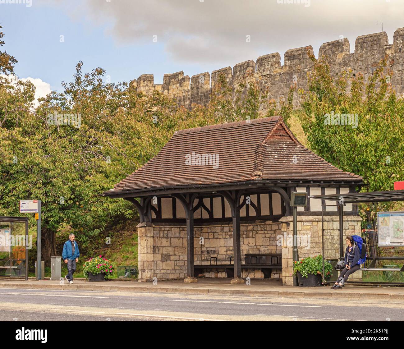 A half-timbered style bus shelter positioned under an ancient city wall ...