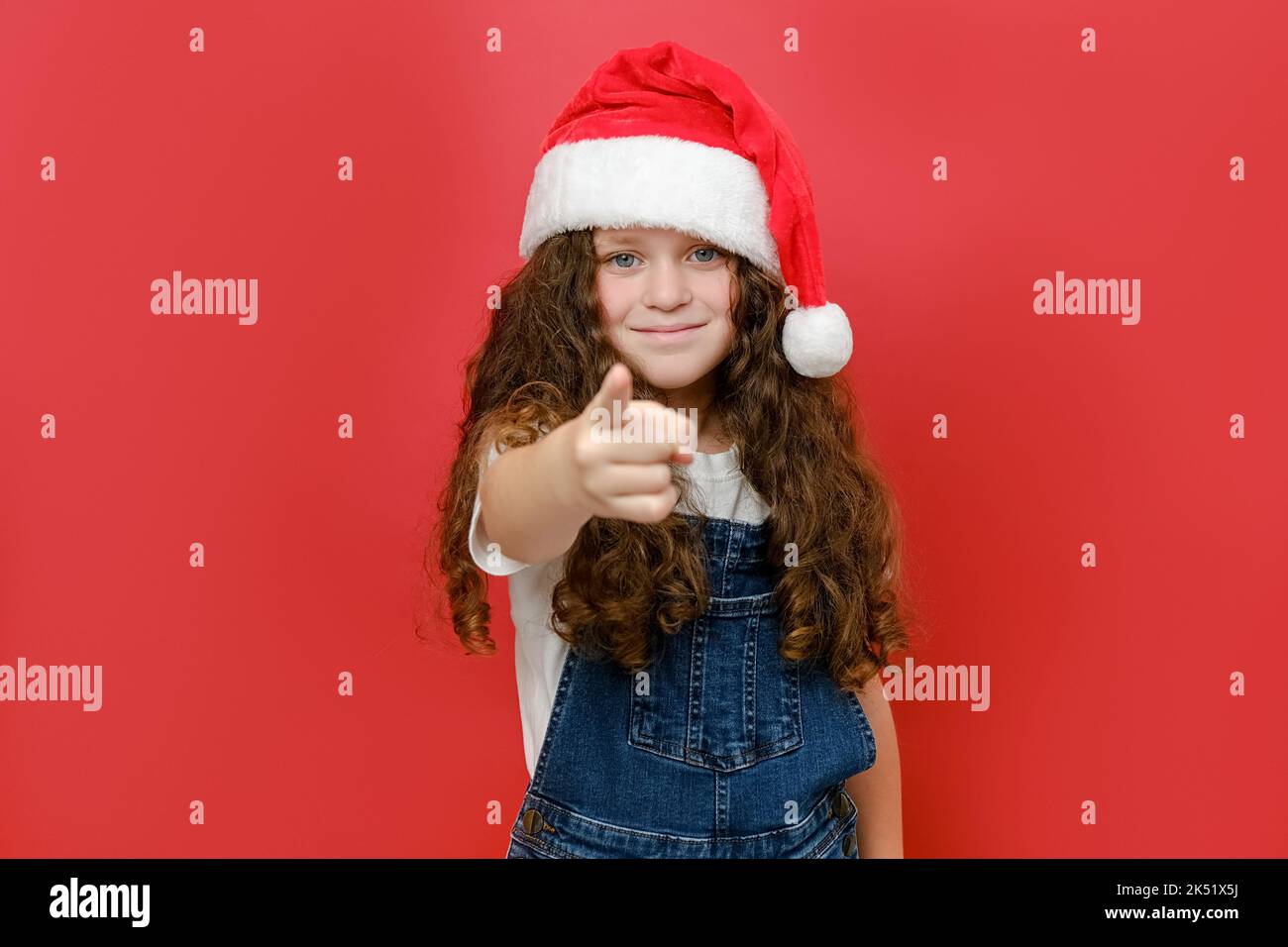 Portrait of smiling little child girl in Santa hat pointing to camera ...