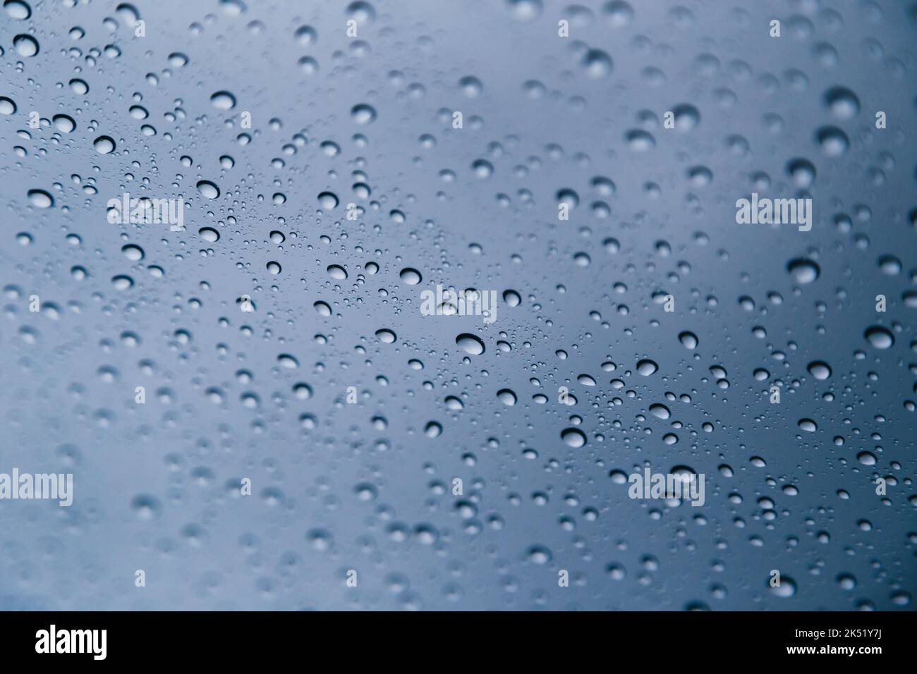 Close up of rain drops on window with blue gray background of dark sky ...