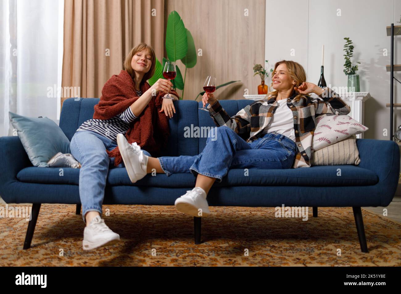 Mother and daughter relaxing on a couch talking while drinking wine ...